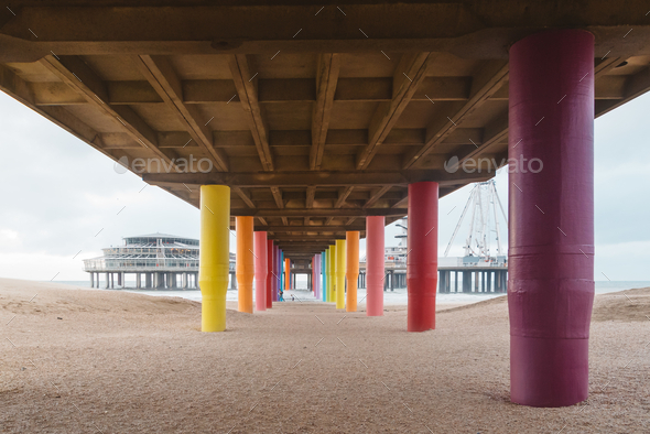Shot under pier with color painted columns on the beach at sunset ...