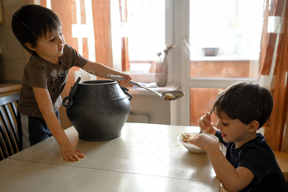 Two boys have lunch at home in the kitchen. One puts food on and the ...