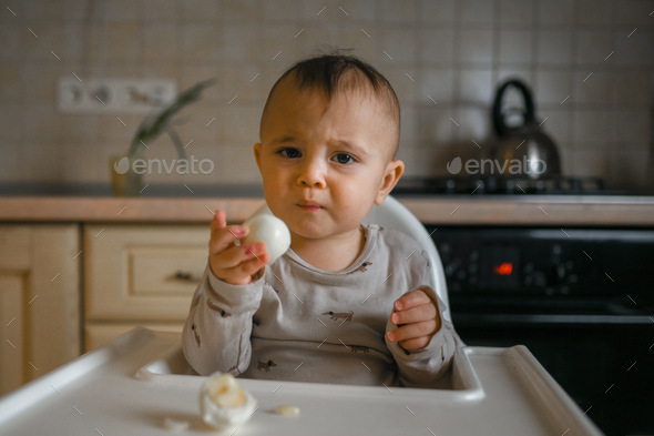 The baby eats a chicken egg at home in the kitchen for breakfast Stock ...