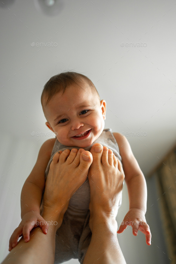 Portrait of a baby. A little boy is hanging on his mother's feet ...