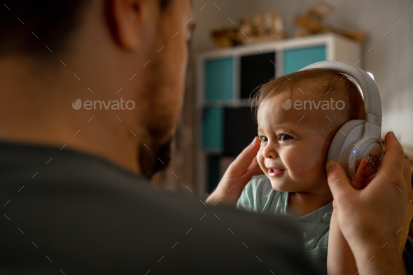 Dad and his little son are listening to music. Dad put on headphones ...