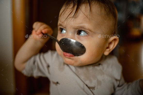 angry kid eats porridge on his own with a big spoon Stock Photo by nastuffa