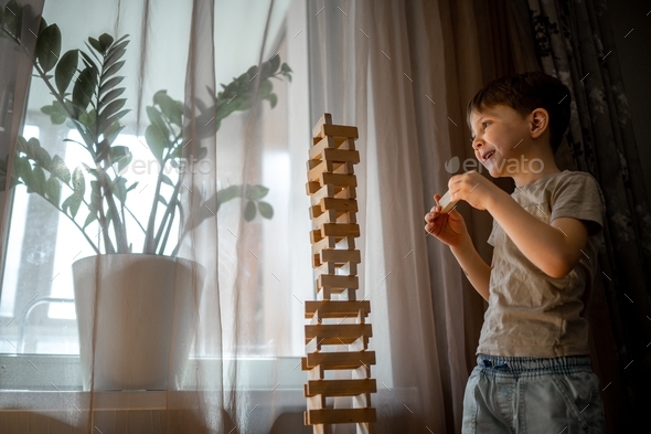 The boy is building a high tower of wooden sticks at home. Stock Photo ...