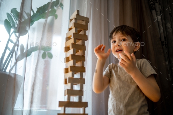 The boy is building a high tower of wooden sticks at home. Stock Photo ...