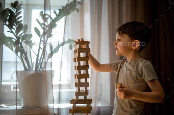 The boy is building a high tower of wooden sticks at home. Stock Photo ...