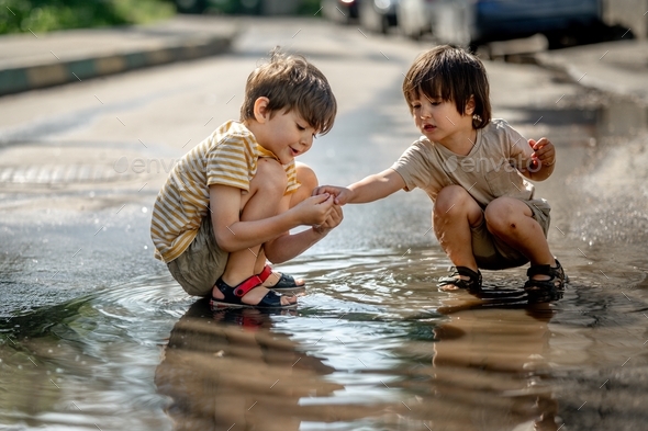 The boys splash in a puddle. Two brothers are walking outside on a hot ...