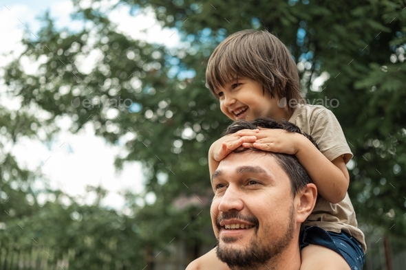 A cute boy is sitting on dad's shoulders. Dad is walking with a child ...