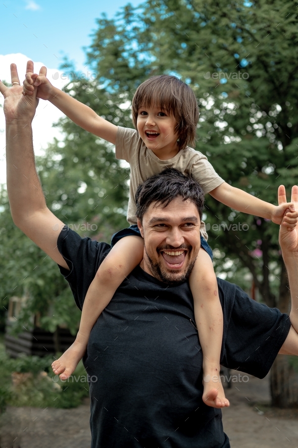A cute boy is sitting on dad's shoulders. Dad is walking with a child ...
