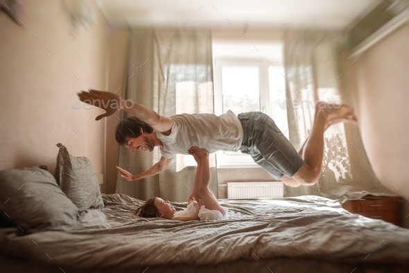 Little daughter having fun with father on the bed. Play aerial acrobats ...