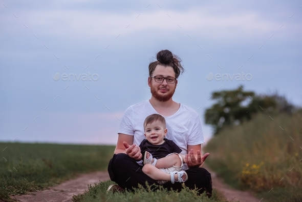 Bearded father with bun of hair on head sits with his one-year-old son ...