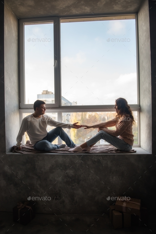 Happy couple in love in winter sweaters, jeans, look and sit opposite ...