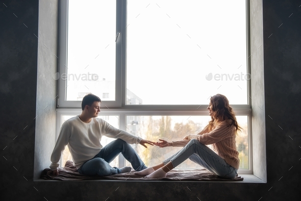 Happy couple in love in winter sweaters, jeans, look and sit opposite ...