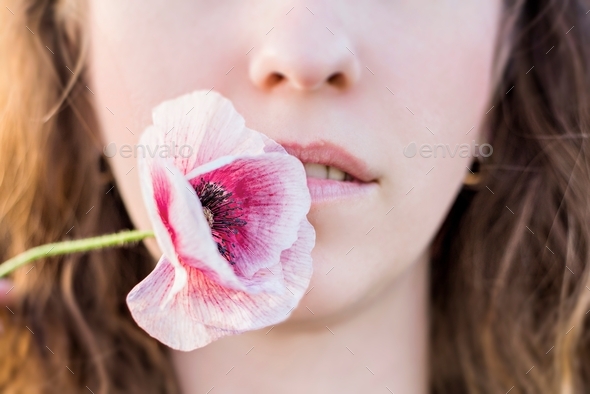 Very close-up portrait of a young woman's face, pink poppy flower near ...