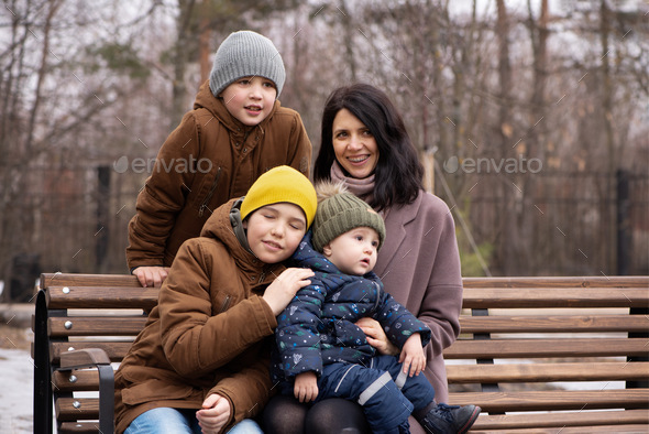 mom and three sons are sitting on a park bench. big happy large family ...