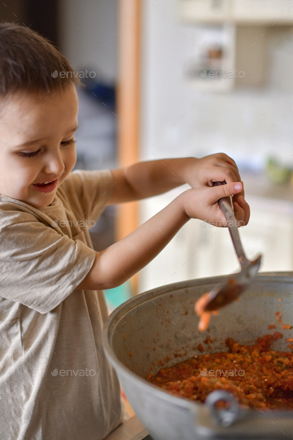 The boy in the kitchen helps his mother cook. The boy is stirring food ...
