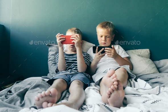 Two schoolboys are sitting on the bed and playing on the phone ...