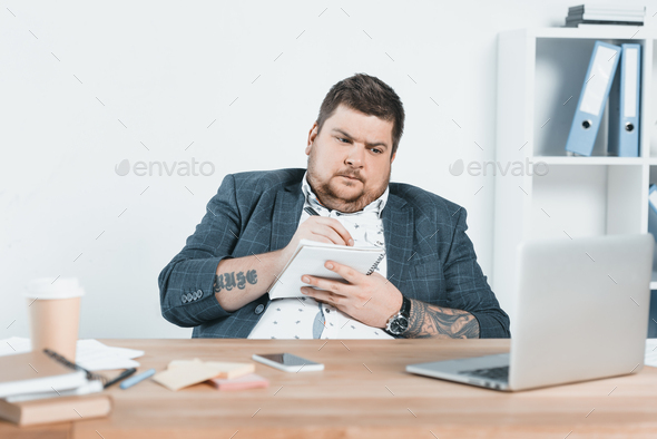 overweight businessman in suit writing in notepad and working with ...