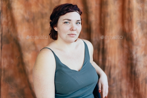 Portrait of a freckled plus size woman. Studio portrait over brown ...