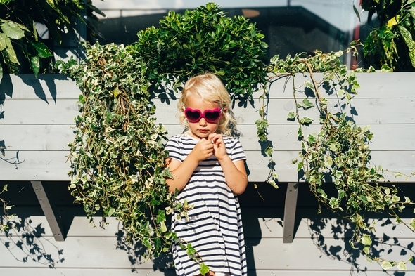 Little pensive sad girl child in summer outside near a wooden wall with ...