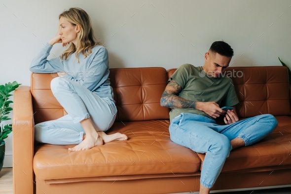 offended wife sits turned away from her husband using a mobile phone ...