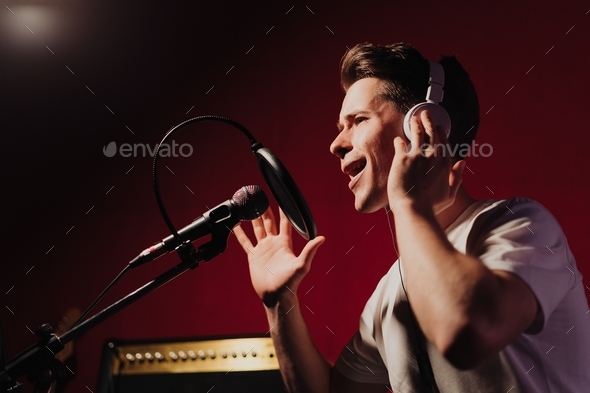 Young man recording a song in an authentic studio on red background ...