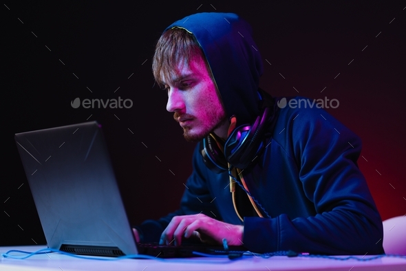 Hacker it genius using laptop writing code wearing hood on head. Cyber ...