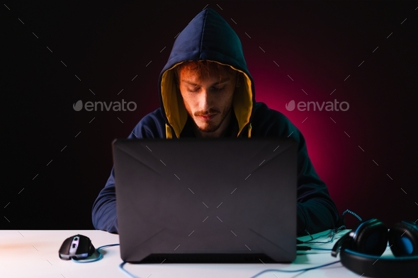 Hacker it genius using laptop writing code wearing hood on head. Cyber ...