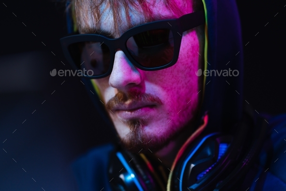 Hacker close up portrait using laptop wearing sunglasses and hood on ...