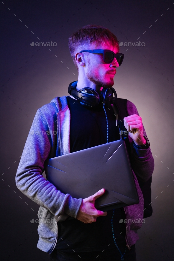 Serious gamer with backpack holding gaming laptop and headsets on dark ...