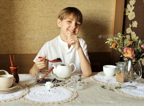A 10-year-old boy pours tea into a teapot at a decorated table at home ...