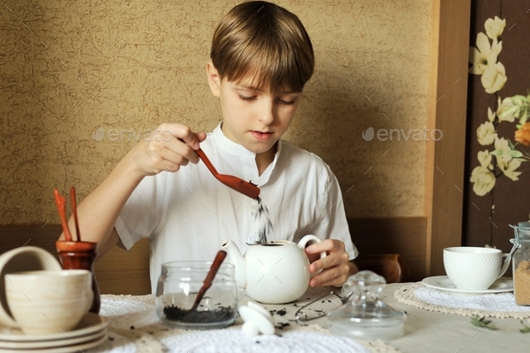 A 10-year-old boy pours tea into a teapot at a decorated table at home ...