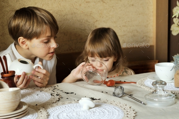 A cute boy and a cute girl are making tea at a beautiful table at home ...