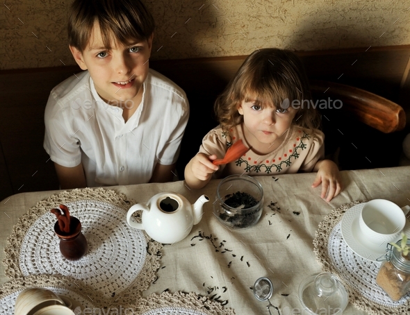 A cute boy and a cute girl are making tea at a beautiful table at home ...