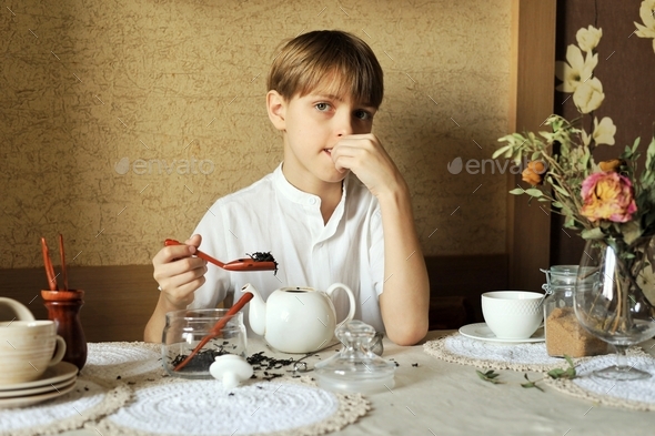 A 10-year-old boy pours tea into a teapot at a decorated table at home ...