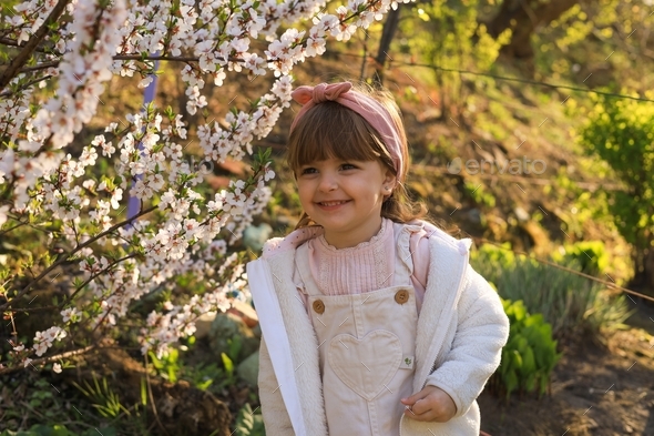 Cute smiling happy girl 2 years is next to a cherry blossom tree in ...