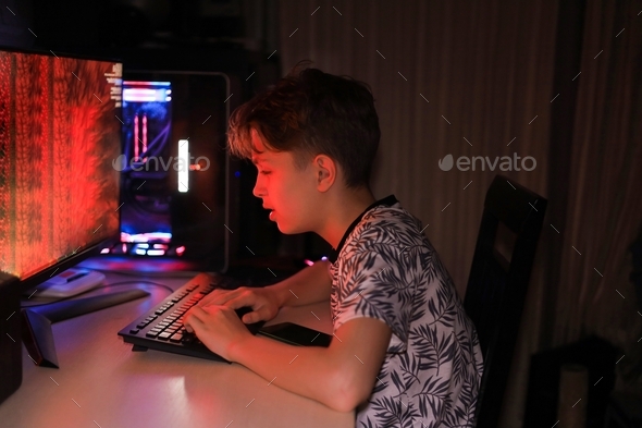 Handsome teenage boy playing computer in the dark using modern ...