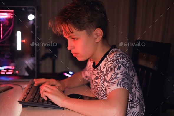 Handsome teenage boy playing computer in the dark using modern ...