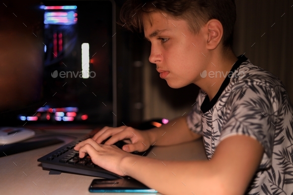 Handsome teenage boy playing computer in the dark using modern ...