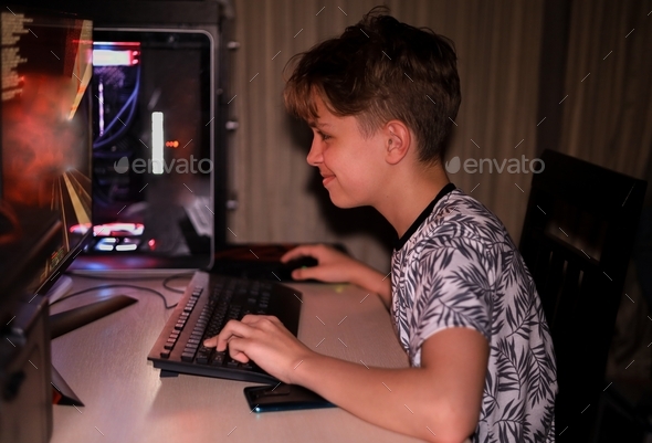 Handsome teenage boy playing computer in the dark using modern ...