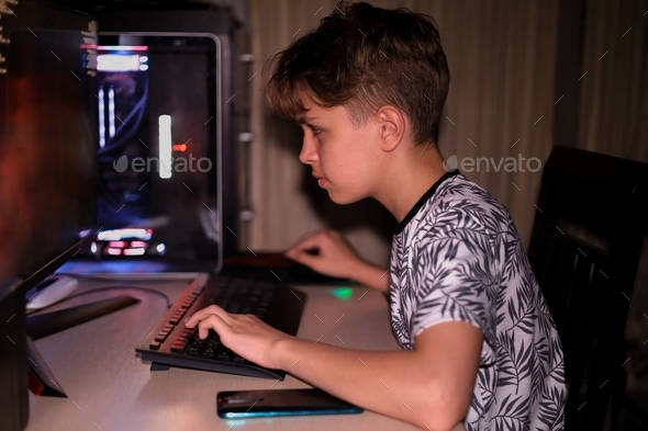 Handsome teenage boy playing computer in the dark using modern ...