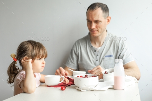 Dad feeds a cute little daughter a healthy breakfast at home on a light ...