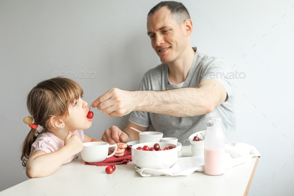 Dad feeds a cute little daughter a healthy breakfast at home on a light ...