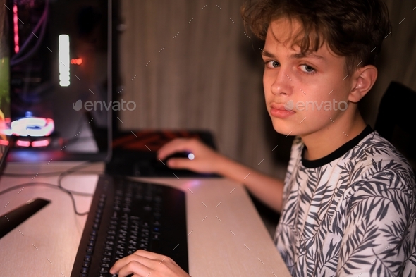 Handsome teenage boy playing computer in the dark using modern ...