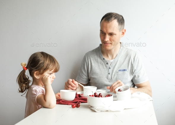 Dad feeds a cute little daughter a healthy breakfast at home on a light ...