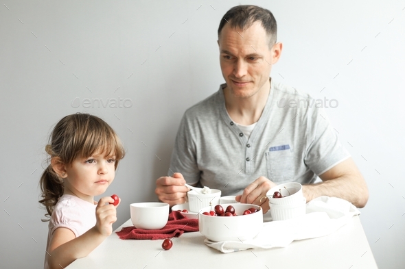 Dad feeds a cute little daughter a healthy breakfast at home on a light ...