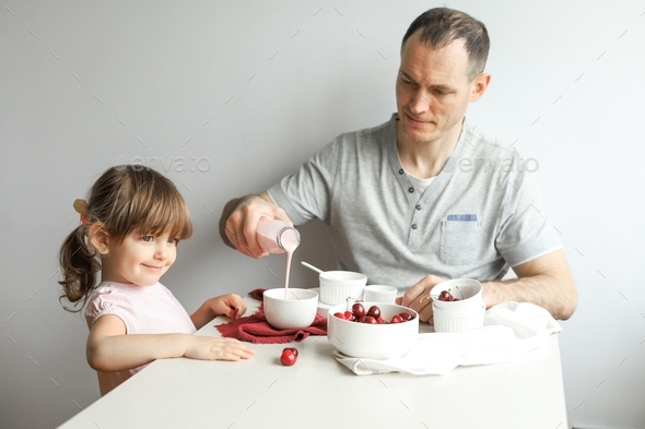 Dad feeds a cute little daughter a healthy breakfast at home on a light ...