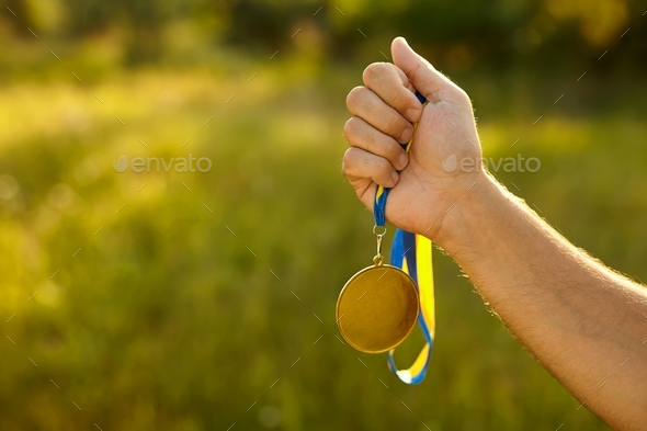 Winner hand holding gold medal with ribbon Stock Photo by InnaVlasova