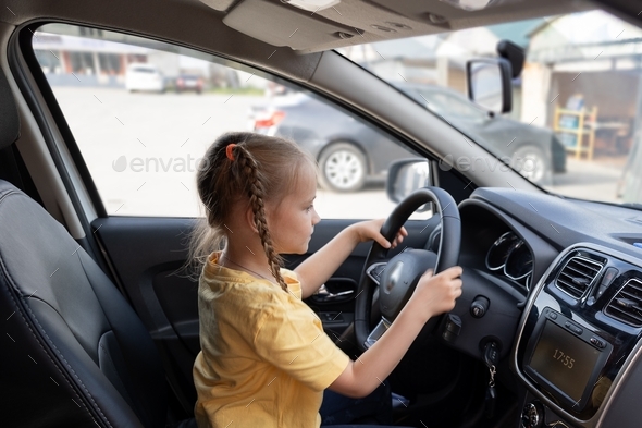 A cute 7-year-old girl is driving a car in the parking lot. Stock Photo ...