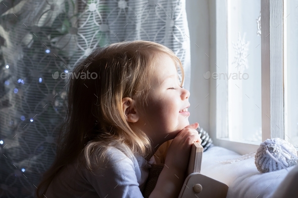 a little girl squeezed her eyes shut from the sunlight from the window ...