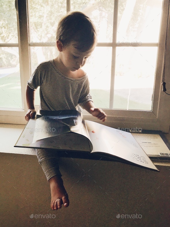 Young boy looking at pictures in a storybook in front of a window #debb ...